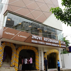 Restaurante com fachada moderna, placa indicando serviço de culinária Indiana, Chinesa, Tandoor e Árabe, e entrada de vidro.