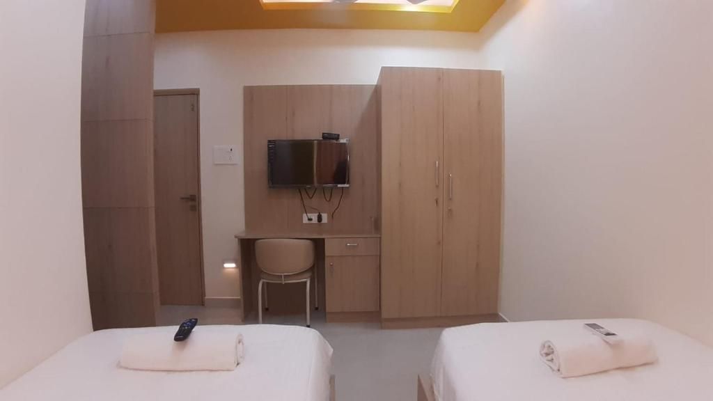 Quarto de hotel com duas camas, uma escrivaninha, uma cadeira e televisão fixada na parede.