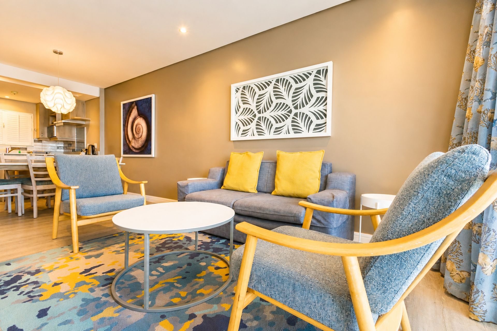 Uma sala de estar moderna com um sofá cinzento, poltronas azuis e uma mesa de centro redonda.