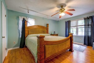 Quarto com cama de madeira, ventoinha no teto e janela com cortinas.