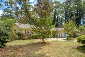 Uma casa de dois andares com um jardim frontal, rodeada por árvores e arbustos.