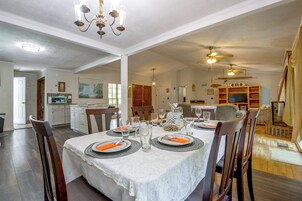 Uma sala de jantar com uma mesa posta para quatro pessoas, cadeiras, um candelabro e um ventilador de teto.