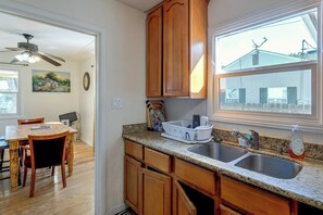 Cozinha com armários de madeira, bancada de granito, pia dupla e janela com vista para uma casa e um moinho de vento.