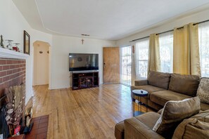 Sala de estar com lareira de tijolos, televisão, sofá e uma janela grande com cortinas.