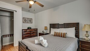 Quarto com cama de madeira, mesa de cabeceira, cômoda, ventilador de teto e uma obra de arte pendurada na parede.