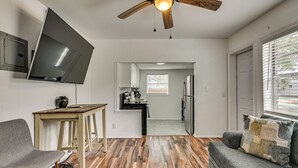 Uma sala de estar moderna com TV de tela plana, ventilador de teto de madeira, sofá e mesa de jantar.