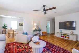 Uma sala de estar moderna com ventilador de teto, televisão de tela plana, espaço de jantar com mesa e cadeiras, e um tapete vermelho vibrante.
