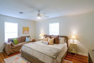 Quarto com cama, sofá, duas mesas de cabeceira com abajures, ventilador de teto e janela com persianas.