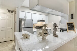 Cozinha moderna com armários brancos, eletrodomésticos de aço inoxidável e esculturas de coral decorativas no balcão.