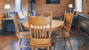 Uma mesa de jantar de madeira com cadeiras, uma televisão fixada na parede e um sofá num quarto com paredes e soalhos de madeira.