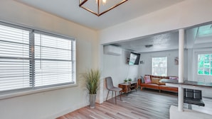 Uma sala de estar espaçosa com piso de madeira, um sofá, uma mesa de jantar e um vaso com planta.