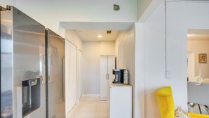 Espaço compacto com cozinha compacta, geladeira, máquina de café e uma poltrona amarela.