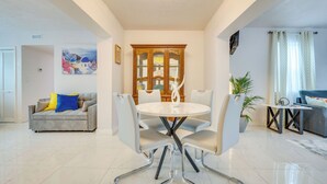 Uma sala de estar moderna com área de jantar, apresentando uma mesa redonda e cadeiras, um sofá e um vaso com planta.