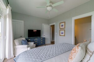 Quarto com cama, televisão, penteadeira e ventoinha no teto.