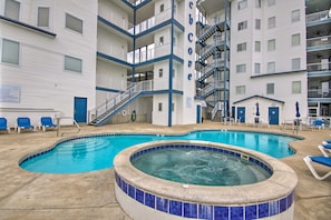Área de piscina com hidromassagem e espreguiçadeiras, rodeada por um edifício com várias andares e varandas.
