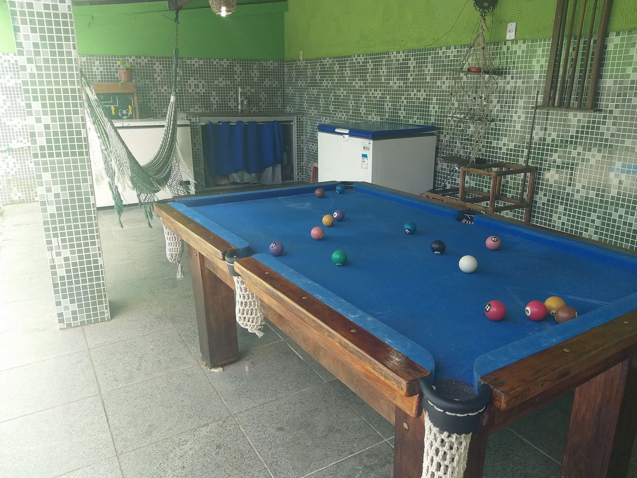 Uma mesa de bilhar com bolas, uma rede e uma parede verde com padrão de azulejos.