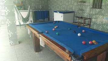 Uma mesa de bilhar com bolas, uma rede e uma parede verde com padrão de azulejos.