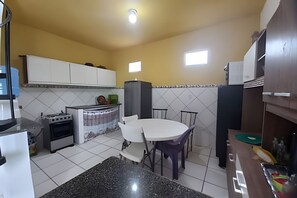 Uma cozinha com armários brancos, fogão, pia e mesa de jantar com cadeiras.