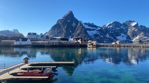 Um fiorde com uma montanha ao fundo, um cais com barcos e edifícios na orla da água.