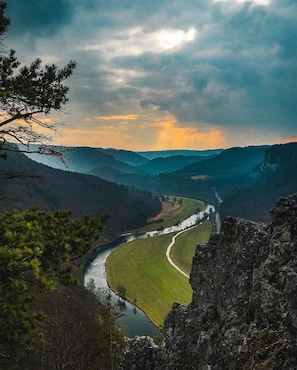 Um rio serpenteando por um vale, com uma estrada sinuosa ao longo dele, cercado por colinas arborizadas.