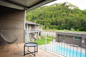 Uma varanda com vista para uma encosta arborizada, uma piscina e uma cadeira.