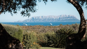 Paisagem costeira com montanha ao fundo, um corpo d'água e barcos.
