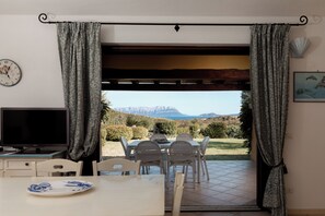 Quarto com mesa de jantar, cadeiras, televisão e cortinas.