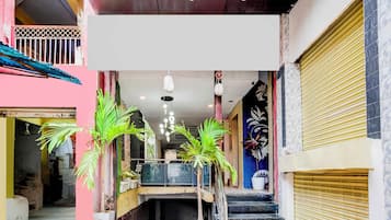 Um edifício comercial com vários andares, uma escada, plantas em vasos e um toldo fechado à direita.