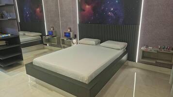 Quarto moderno com cama grande, mesa de cabeceira, TV fixada na parede e decoração com tema de galáxia.