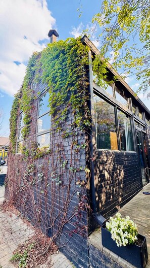 Um edifício com fachada de tijolos, parcialmente coberto por plantas trepadeiras.