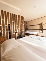 Quarto de hotel com uma cama grande, uma escrivaninha e uma cadeira. Apresenta um painel de parede em madeira e um espelho.