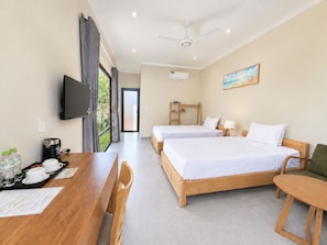 Quarto de hotel com duas camas, uma mesa de jantar, uma TV e um quadro na parede.