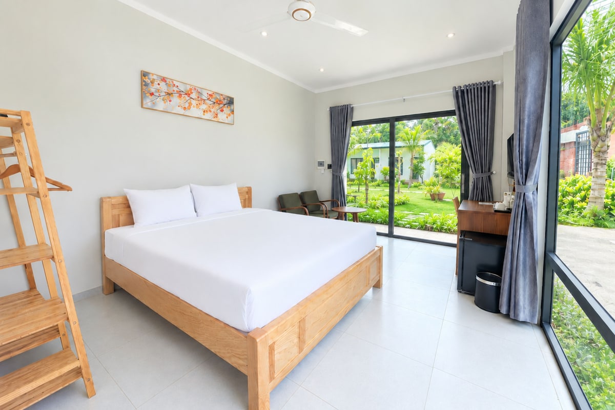 Quarto de hotel com cama grande, escada de madeira, escrivaninha com cadeira e vista para o exterior através de uma porta de vidro.