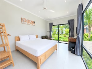 Quarto de hotel com cama grande, escada de madeira, escrivaninha com cadeira e vista para o exterior através de uma porta de vidro.