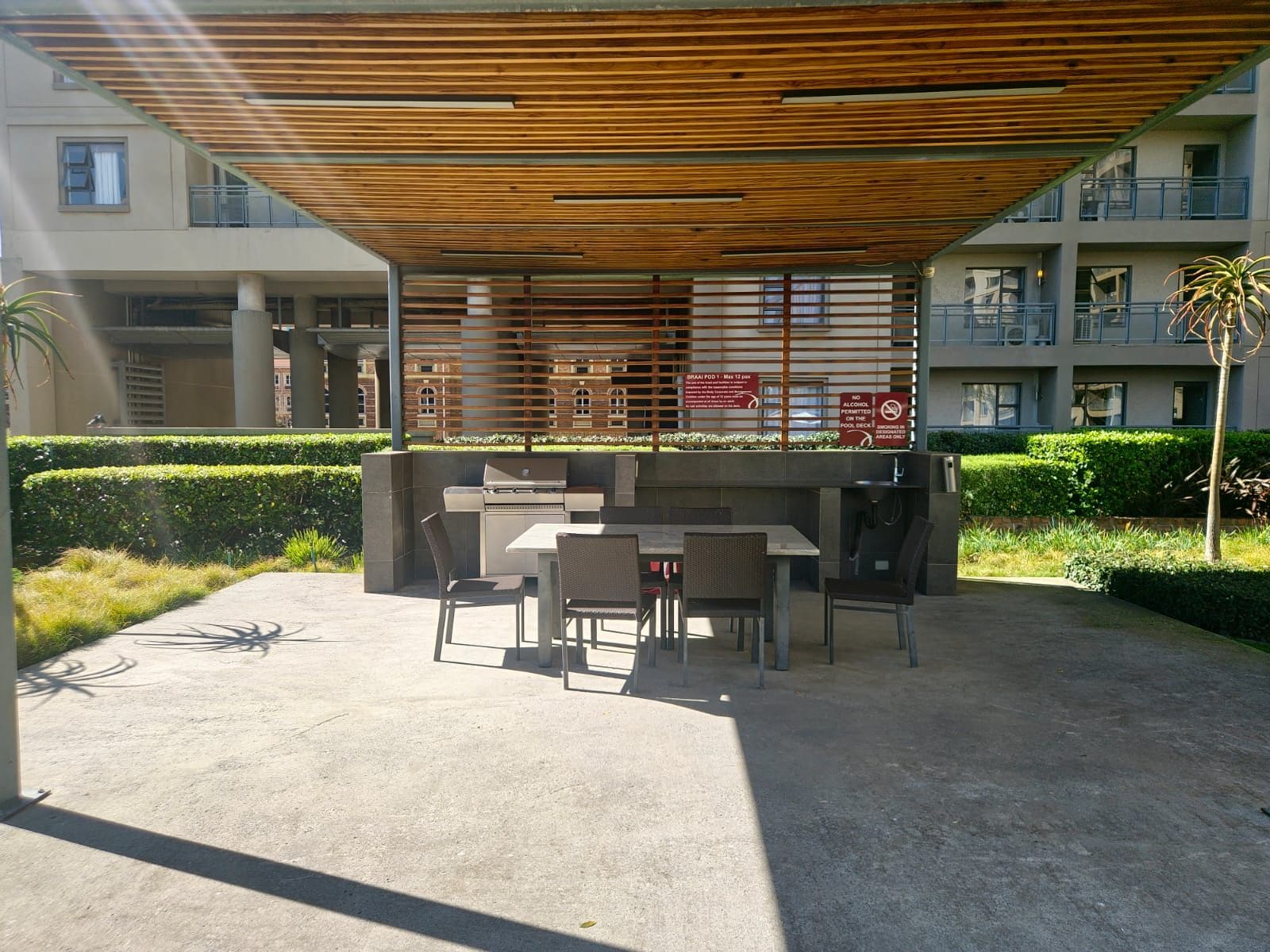 Área de varanda externa com estação de churrasco, assentos e vista para um prédio ao fundo.