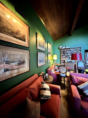 Quarto aconchegante com paredes verdes, teto de madeira e um espaço de estar com sofás vermelhos e uma pequena mesa redonda.