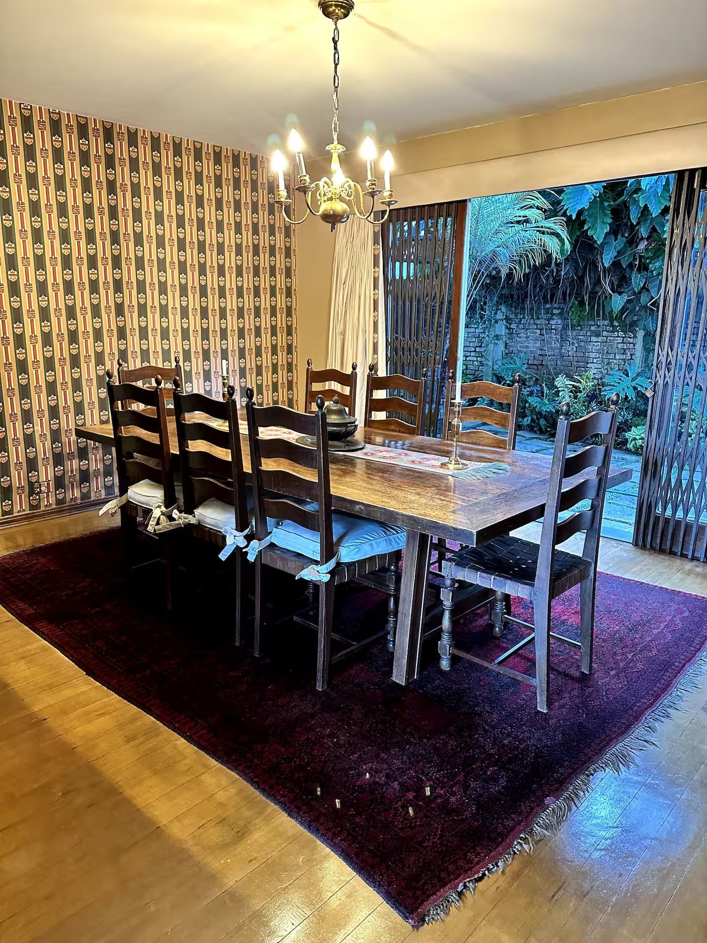 Uma sala de jantar com mesa e cadeiras de madeira, um lustre e papel de parede estampado.
