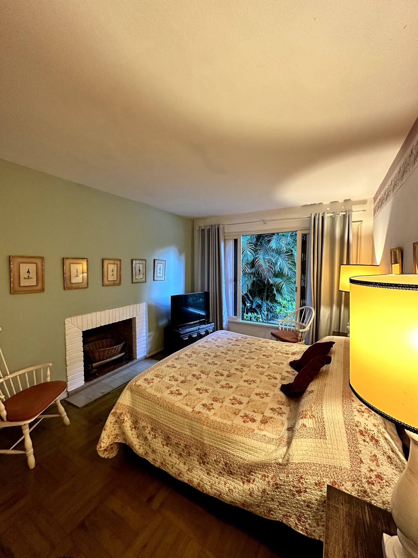 Quarto com cama grande, lareira, televisão e janela com cortinas.