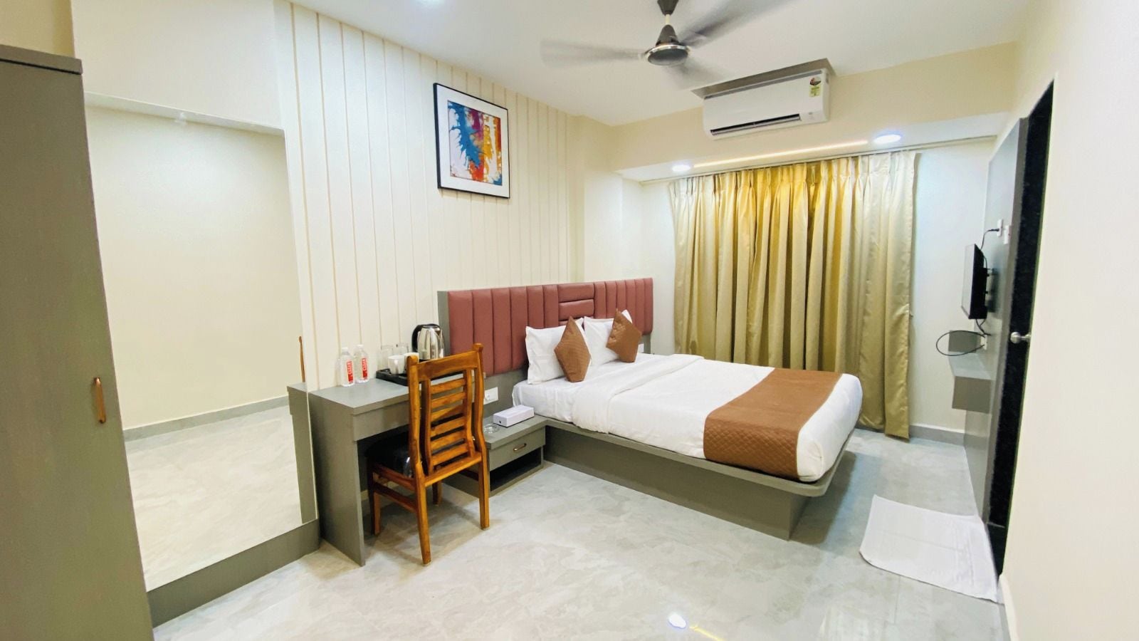 Quarto de hotel com cama, escrivaninha, cadeira e ventoinha no teto.