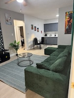 Uma sala de estar moderna com um sofá verde, uma mesa de centro de vidro e um tapete estampado.