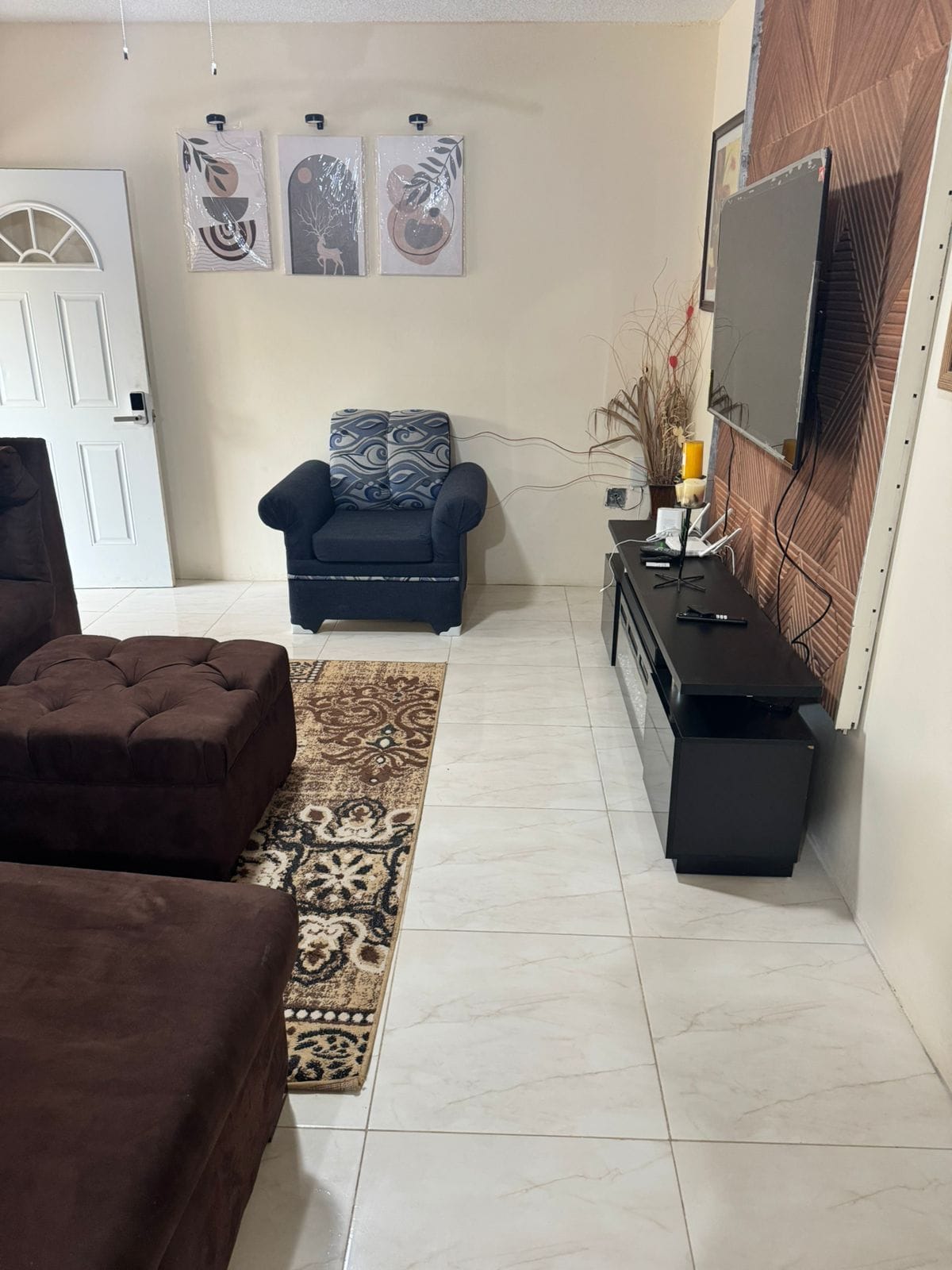 Uma sala de estar com sofá, poltrona, mesa de centro, televisão e quadros nas paredes.