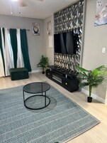 Uma sala de estar moderna com televisão de tela plana, um rack preto, uma mesa de centro redonda e duas plantas em vasos.