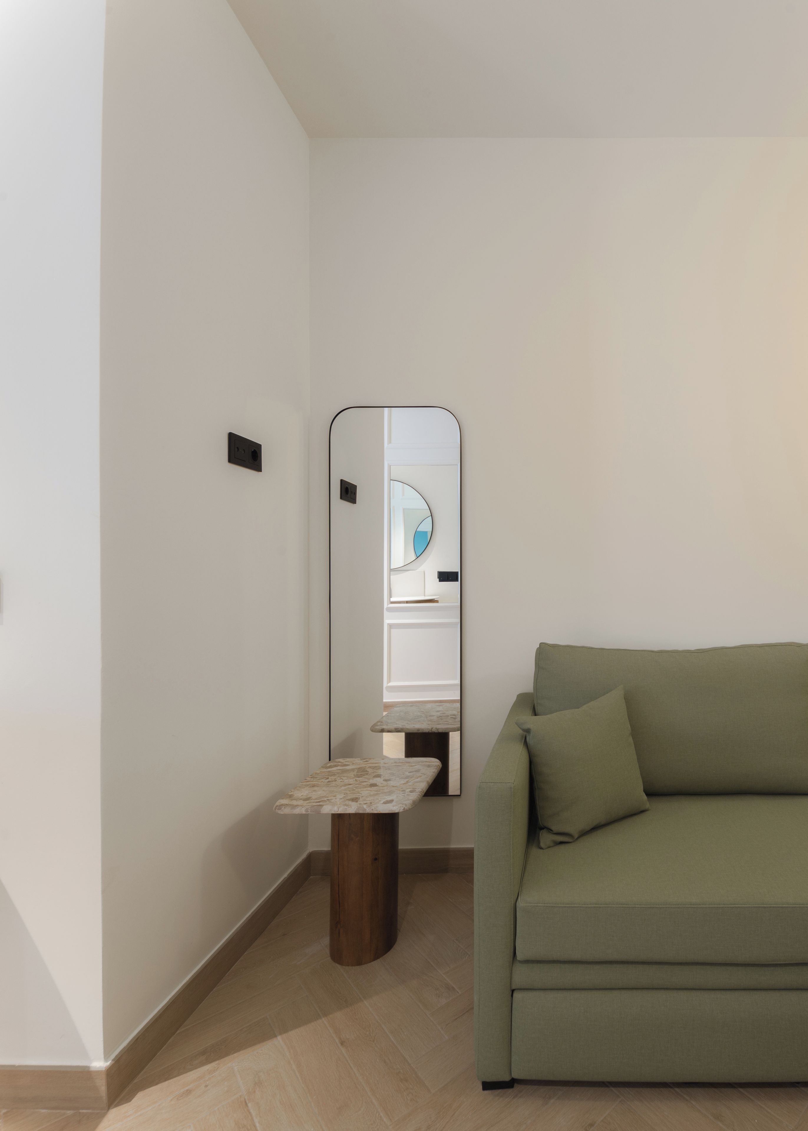 Sala de estar minimalista com um sofá verde, uma mesinha de madeira e um espelho na parede.