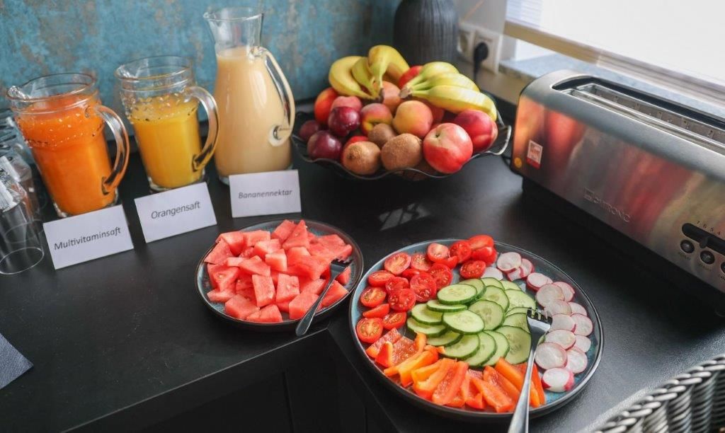 Buffet de café da manhã com diversas frutas, legumes e sucos.