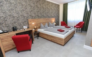 Quarto de hotel moderno com cabeceira de madeira, escrivaninha, cadeira, cama com almofadas e televisão.