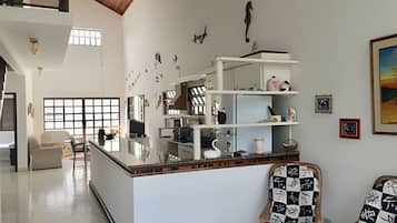 Uma sala de estar espaçosa com uma ilha central, uma área de jantar com cadeiras e uma cozinha com armários brancos.