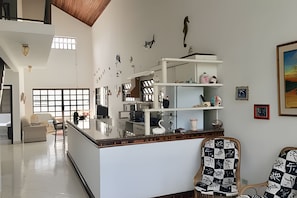 Uma sala de estar espaçosa com uma ilha central, uma área de jantar com cadeiras e uma cozinha com armários brancos.