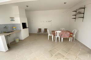 Cozinha com bancada, pia e uma pequena janela. Há uma área de refeições com mesa e cadeiras.