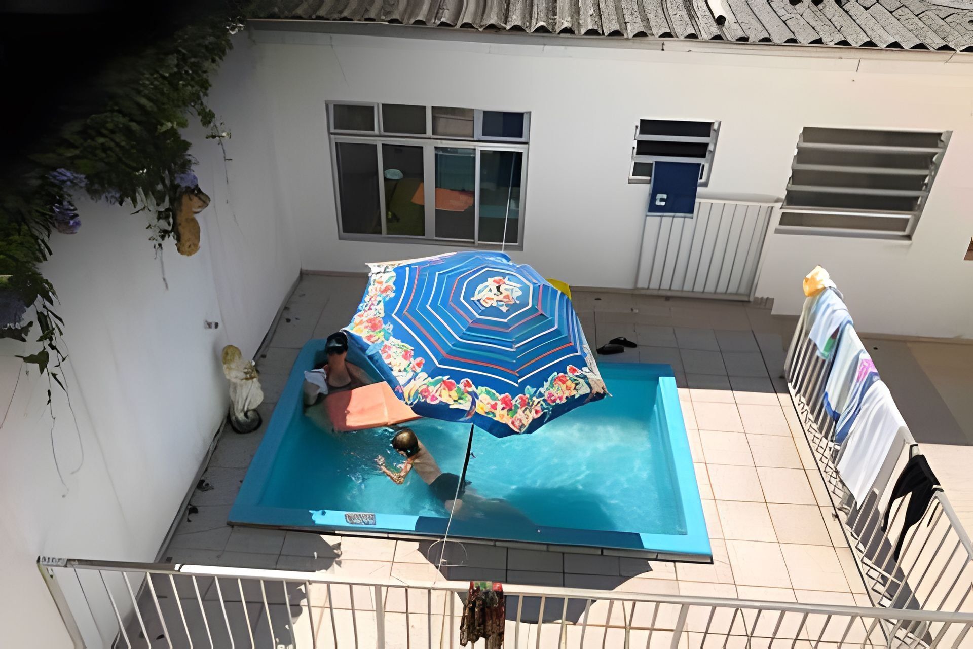 Uma piscina com um guarda-sol colorido, uma parede branca e uma janela.