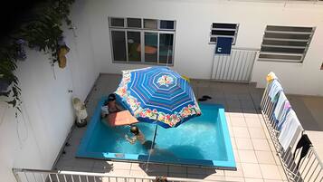 Uma piscina com um guarda-sol colorido, uma parede branca e uma janela.